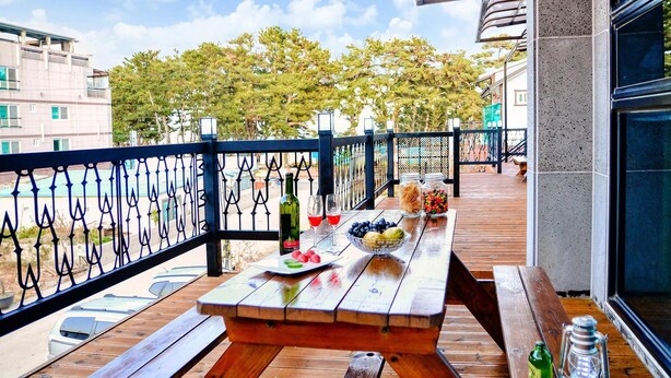 Um deck de madeira com uma mesa posta para uma refeição, incluindo copos de vinho, uma garrafa e uma tigela de frutas.