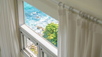 Janela com vista para o oceano e vegetação.