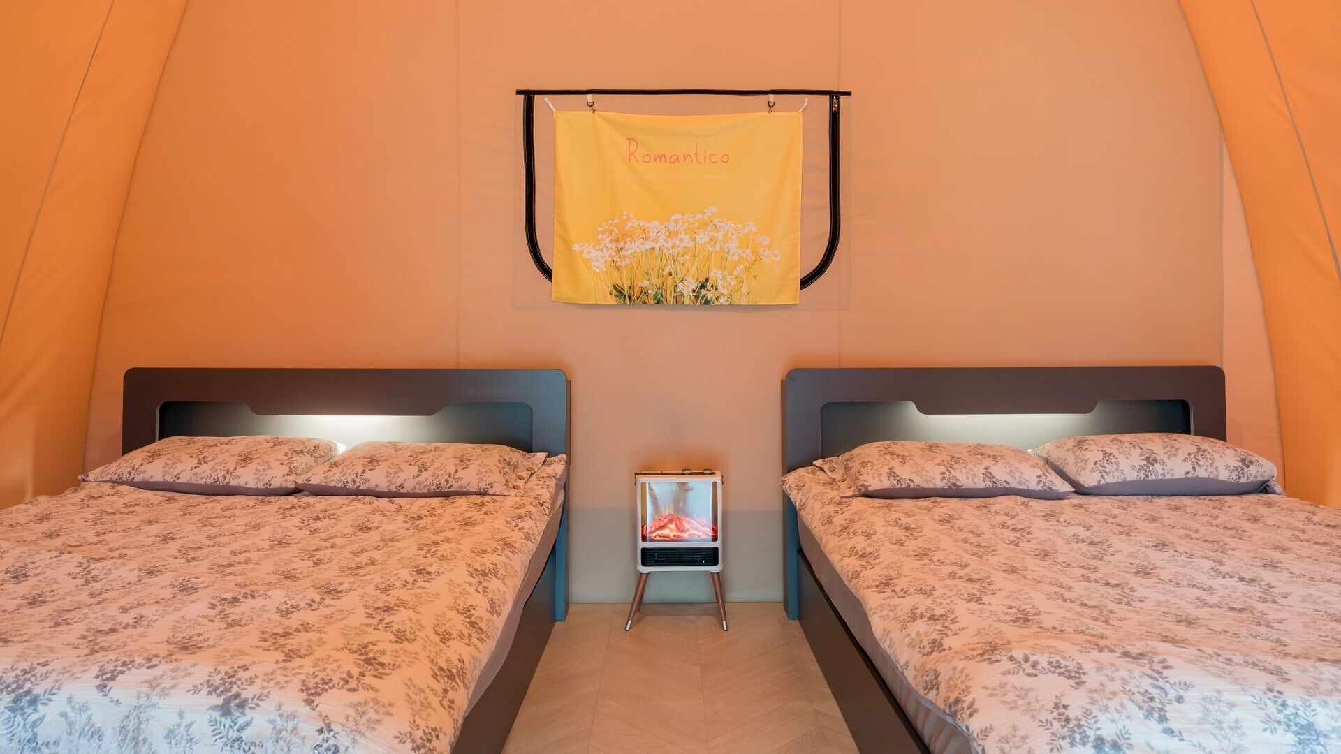 Quarto com duas camas, uma mesa pequena com um aquecedor e um painel de parede com a palavra 'Romantico'.