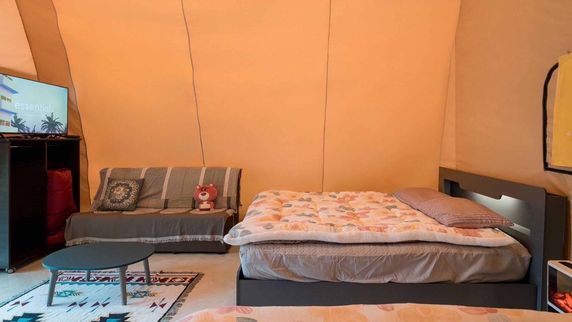 Um quarto com cama, sofá, televisão e uma mesinha.