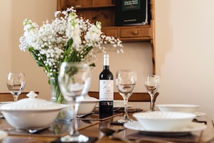 Uma mesa de jantar posta com pratos brancos, uma garrafa de vinho e um vaso de flores.