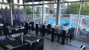 Restaurante com mesas e cadeiras ao ar livre, vista para uma piscina e área cercada com vegetação.