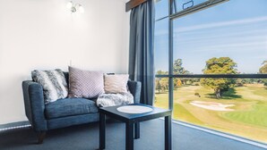 Uma sala de estar moderna com um sofá cinzento, vários almofados, uma mesinha redonda e uma grande janela com vista para um campo de golfe.