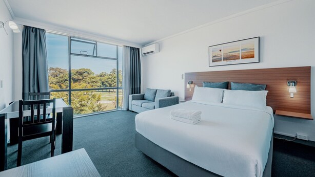 Quarto de hotel com uma cama grande, uma escrivaninha, uma cadeira e vista para árvores e um campo de golfe pela janela.