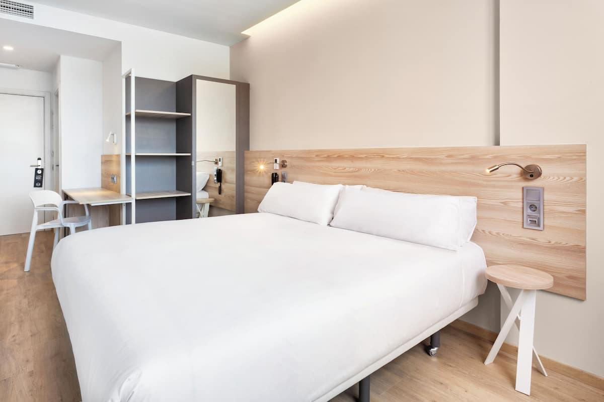 Quarto de hotel moderno com uma cama grande, uma escrivaninha e um guarda-roupa.
