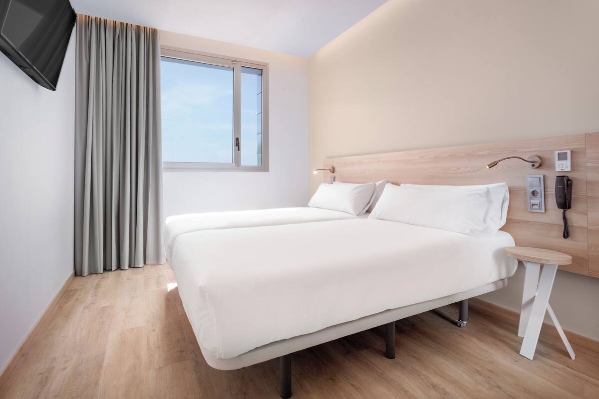 Quarto de hotel com cama grande, mesa de cabeceira e televisão na parede.