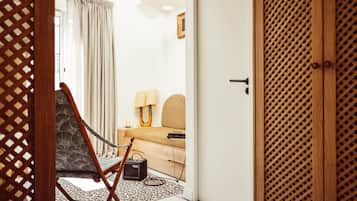 Um quarto com piso de madeira, um tapete estampado, um sofá, uma luminária e um alto-falante.