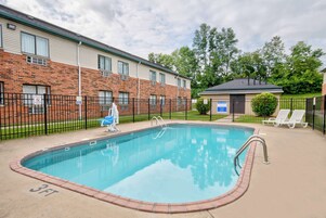 Piscina com marcação de profundidade de 3 pés, rodeada por um edifício de tijolos, área cercada e espreguiçadeiras.