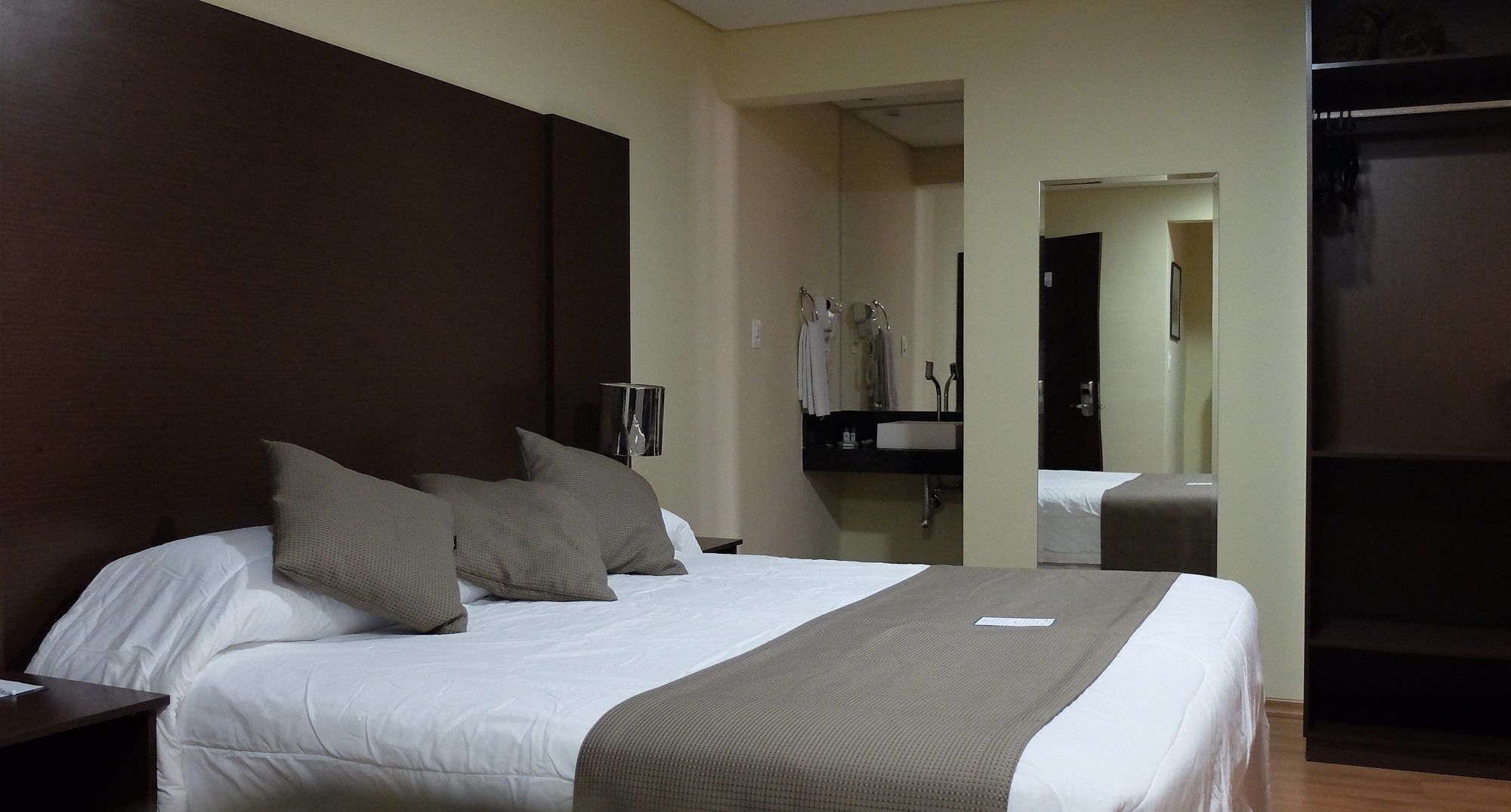 Quarto de hotel com uma cama grande, mesa de cabeceira, espelho e guarda-roupa.