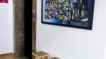 Um corredor com piso ladrilhado, uma porta e uma pintura abstrata emoldurada na parede.