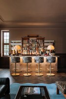 Uma área de bar com balcão, banquetas e diversos frascos e copos.