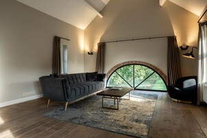 Uma sala de estar ampla com um sofá moderno, uma mesa de centro e uma grande janela em arco com vista para o verde lá fora.