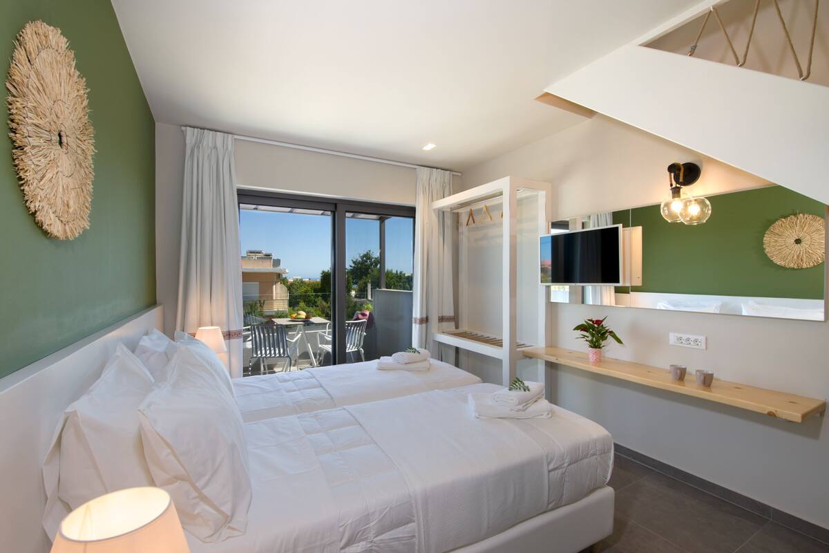 Quarto de hotel moderno com uma cama grande, televisão, varanda com vista e uma pequena planta numa prateleira.