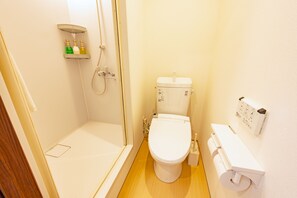 Uma casa de banho pequena com sanita, chuveiro e um prateleira com artigos de higiene pessoal.