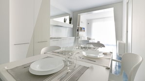Uma zona de refeições moderna com uma mesa branca posta para quatro pessoas, incluindo pratos, copos e talheres.