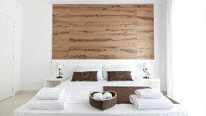Quarto de hotel moderno com uma cama grande, roupa de cama branca, duas mesas de cabeceira com abajures e uma cabeceira de madeira.