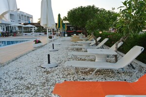 Uma área na beira da piscina com espreguiçadeiras, guarda-sóis e um edifício ao fundo.
