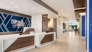 Uma área de recepção de hotel com design moderno, incluindo um balcão de atendimento, uma parede geométrica azul e branca, e uma parede de destaque em madeira.