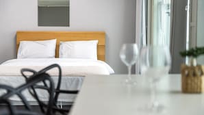 Cama bem arrumada com roupa de cama e almofadas brancas, cabeceira de madeira e mesa de cabeceira com um copo e uma planta.