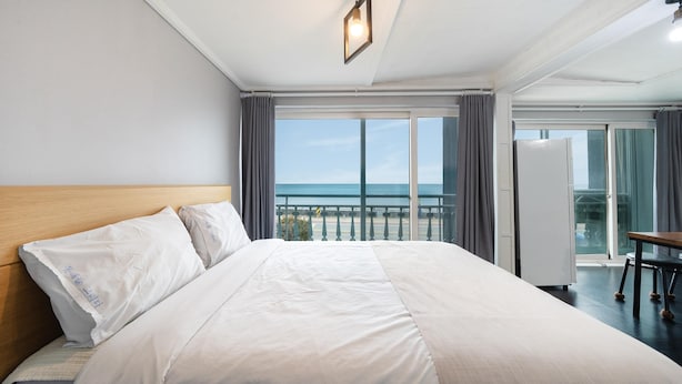 Quarto de hotel com uma cama grande, cabeceira de madeira, varanda com vista para o mar e um frigorífico.