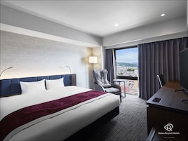 Quarto de hotel com cama, escrivaninha, cadeira e vista para a cidade.