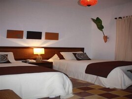 Quarto de hotel com duas camas, uma mesinha de cabeceira com abajur e uma planta presa à parede.