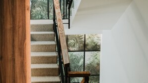 Escadaria moderna com corrimão de madeira, um vaso de planta e vista de um jardim interno exuberante.