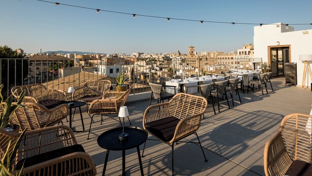 Terraço no telhado com móveis de vime, mesas e cadeiras, com vista para a paisagem urbana.