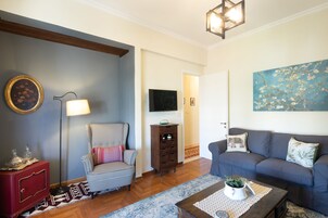 Uma sala de estar com uma poltrona xadrez, um sofá azul, um armário de madeira e um abajur.