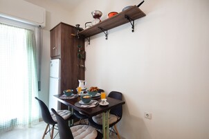 Uma sala de jantar com mesa posta para dois, um refrigerador e uma prateleira acima da mesa.