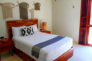 Cama bem arrumada com cabeceira de madeira, mesa de cabeceira com uma tigela e tapeçarias de macramé na parede.