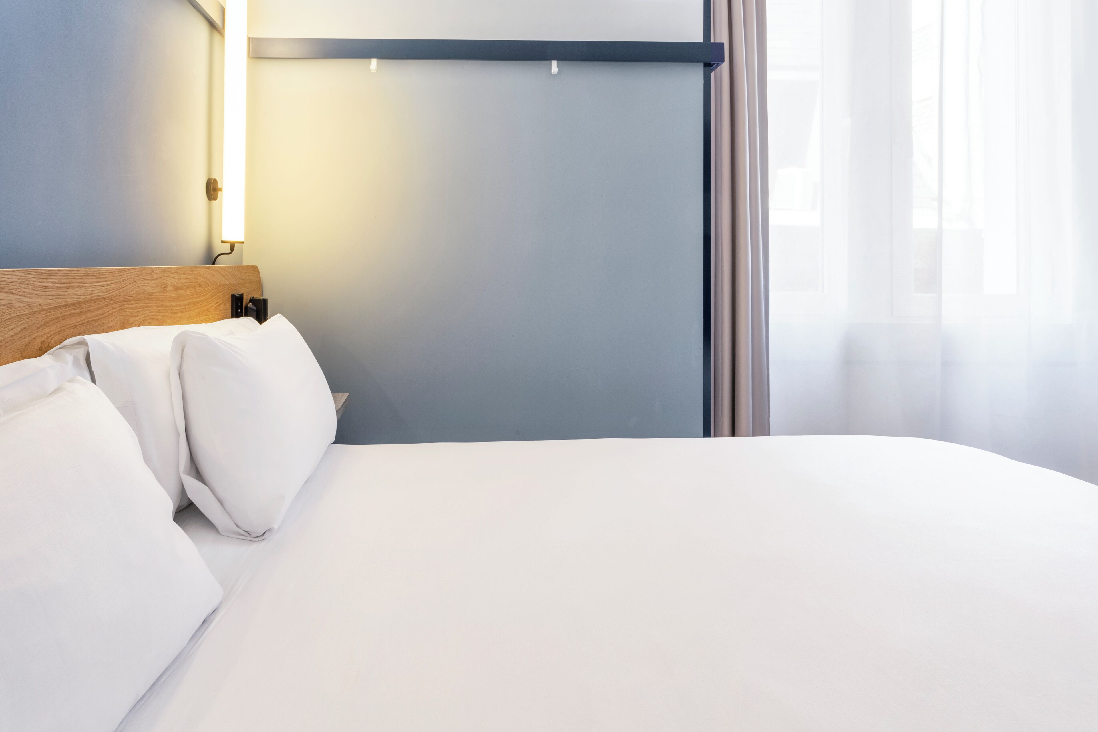 Cama bem arrumada com lençóis brancos num quarto de hotel moderno.