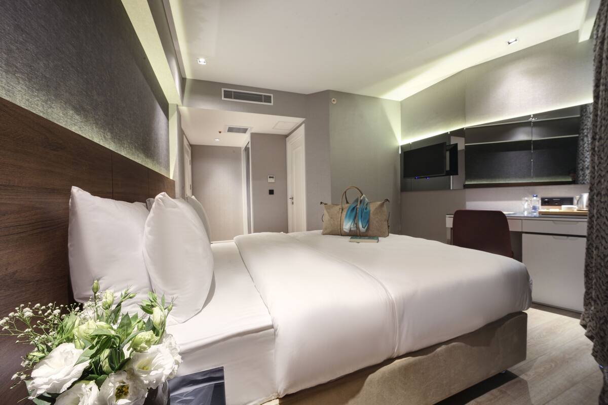 Quarto de hotel com uma cama grande, uma escrivaninha, uma televisão e a porta do banheiro.