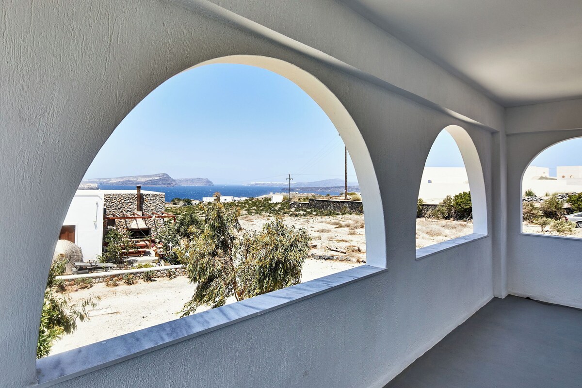 Quarto com três janelas em arco que oferecem vista para uma paisagem costeira, incluindo edifícios e vegetação.