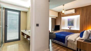 Quarto de hotel moderno com cama, mesa de cabeceira, televisão e uma janela grande com persianas.