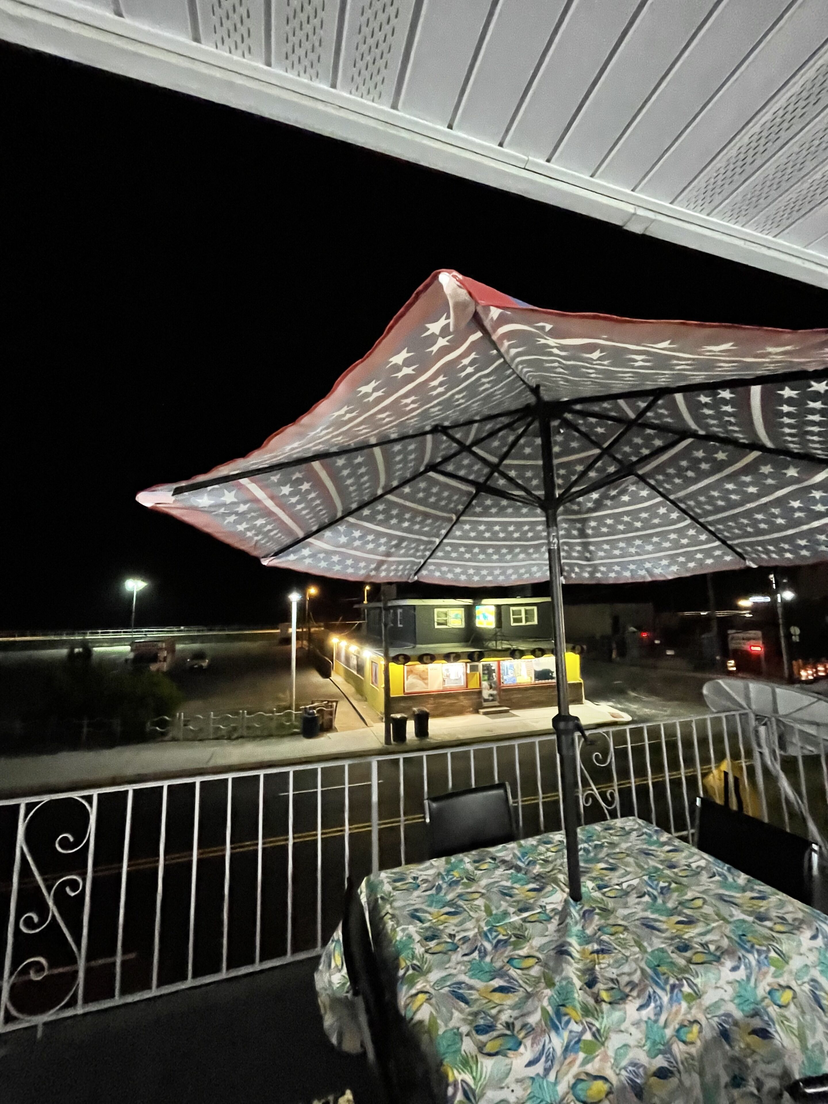 Uma varanda com mesa, cadeiras, guarda-sol e vista para um edifício iluminado.