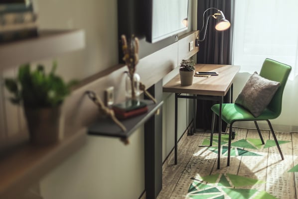 Quarto moderno com escrivaninha de madeira, cadeira verde, luminária e planta em vaso.