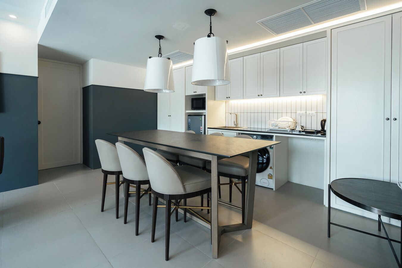 Uma cozinha moderna com ilha central, armários brancos e iluminação pendente.