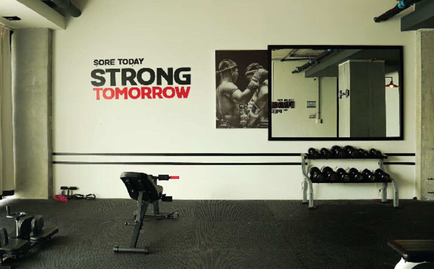 Uma academia com pôster motivacional, equipamentos de ginástica e um espelho.