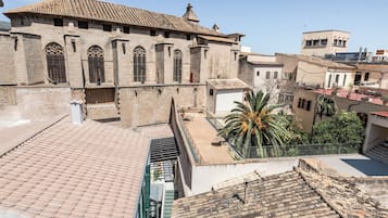 Um edifício histórico com janelas em arco e telhado telhado, rodeado por outros edifícios e uma palmeira.