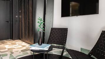 Um interior moderno com esquema de cores preto e branco, apresentando um tapete redondo, duas poltronas confortáveis, uma mesa pequena com um vaso e livros, e uma TV de tela plana fixada na parede.