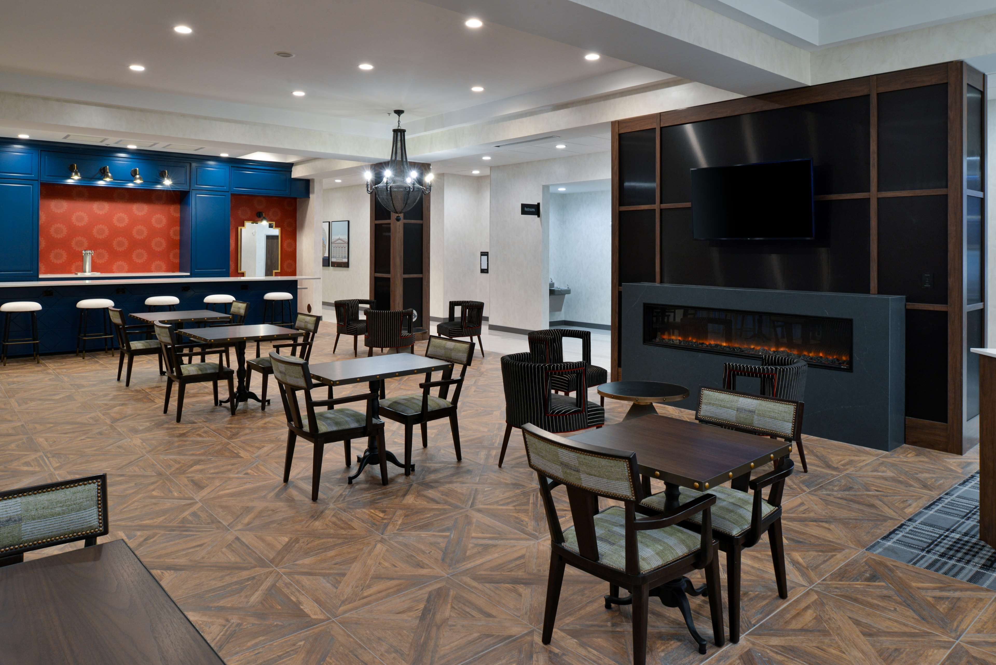 Uma ampla sala de jantar com várias mesas e cadeiras, um espaço bar com banquetas e uma lareira moderna.