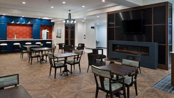 Uma ampla sala de jantar com várias mesas e cadeiras, um espaço bar com banquetas e uma lareira moderna.