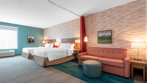 Quarto de hotel com cama, sofá, um banquinho redondo, mesa de cabeceira e luminária fixada na parede.