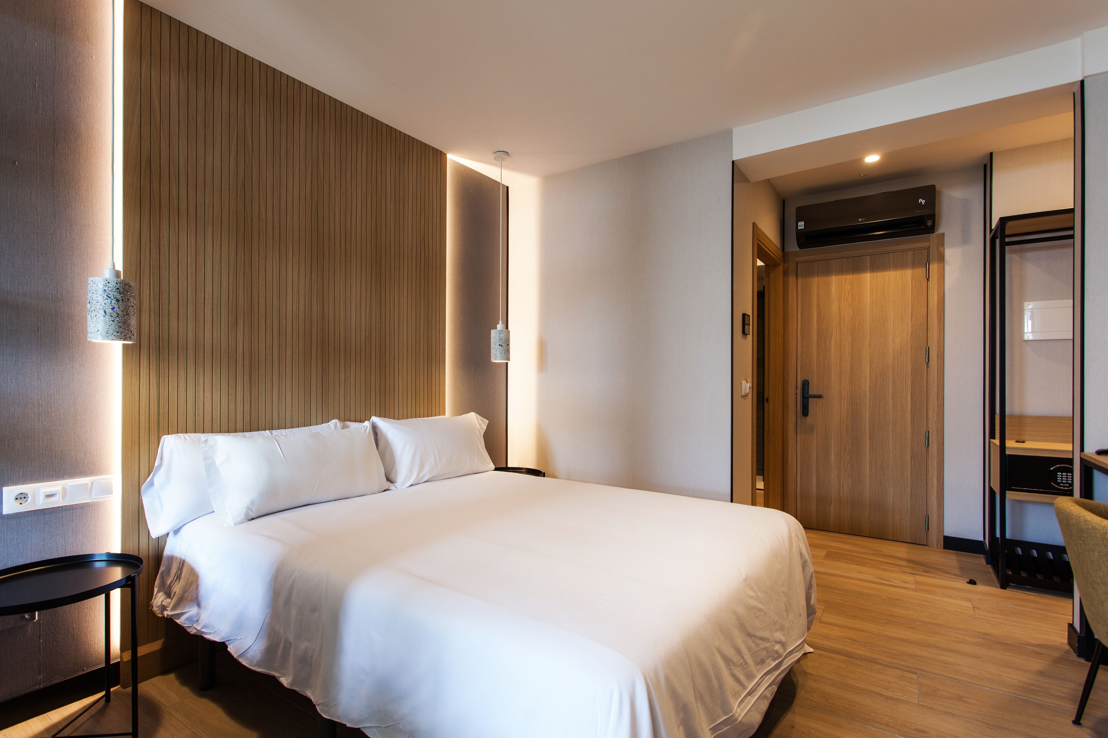 Quarto de hotel com uma cama grande, painel de parede de madeira, uma escrivaninha com cadeira e um guarda-roupa.