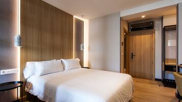 Quarto de hotel com uma cama grande, painel de parede de madeira, uma escrivaninha com cadeira e um guarda-roupa.