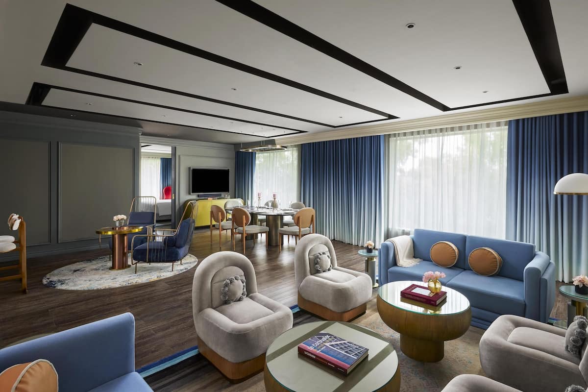 Uma sala de estar moderna com um sofá azul, poltronas, uma mesa de centro e uma área de jantar com televisão e conjunto de mesa e cadeiras.