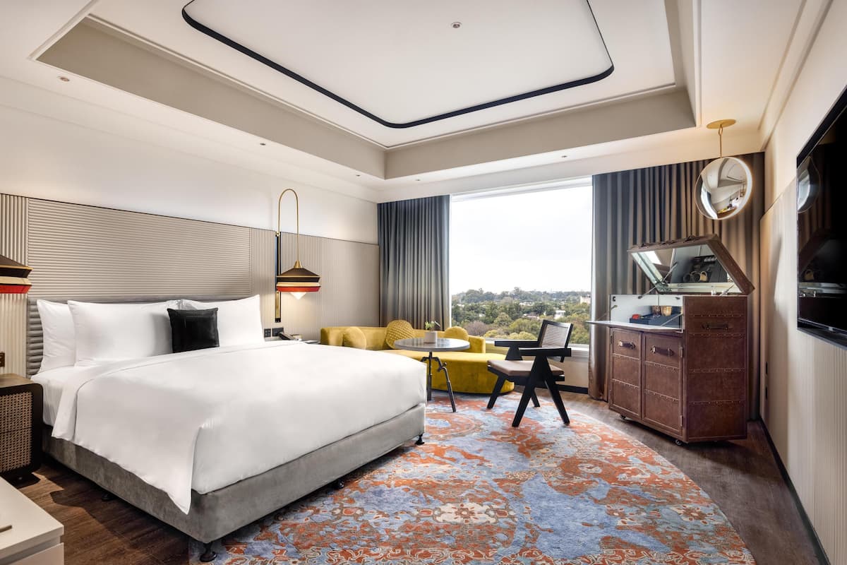 Quarto de hotel moderno com uma cama grande, um sofá, uma mesinha e uma televisão.