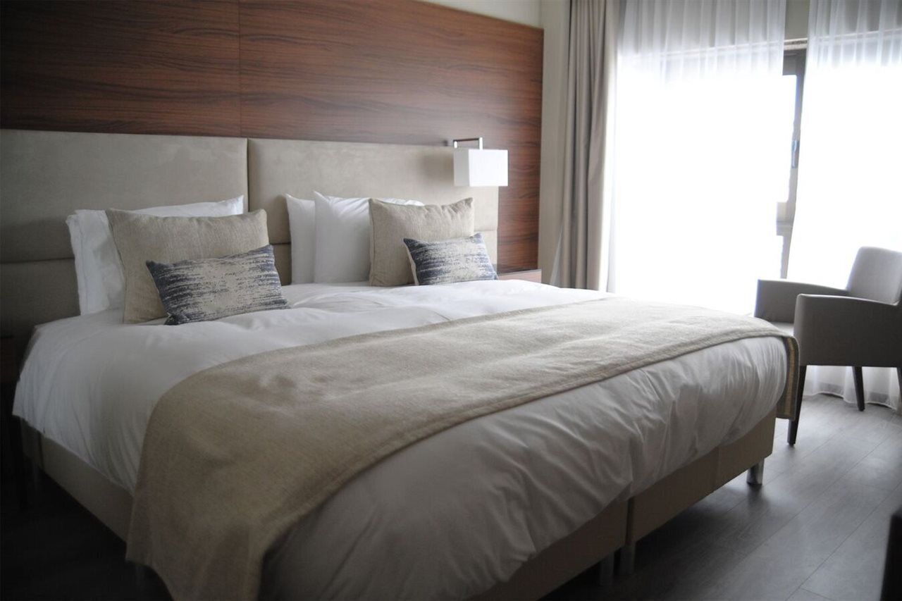 Uma cama grande com cabeceira de madeira, vários travesseiros e uma mesa de cabeceira com abajur.