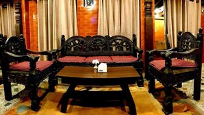 Quarto tradicional com sofá, duas poltronas, mesa de centro de madeira e tapete estampado.
